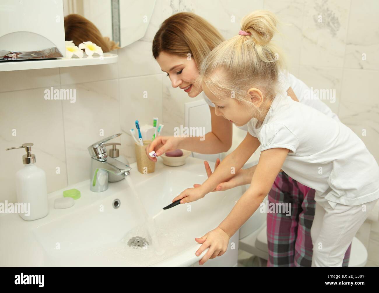 Little girl with her mother brushing teeth near sink in bathroom Stock ...