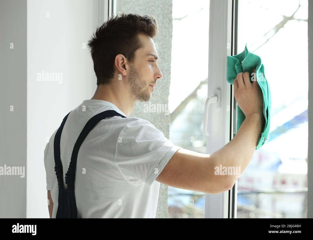 Young man cleaning window in office Stock Photo - Alamy