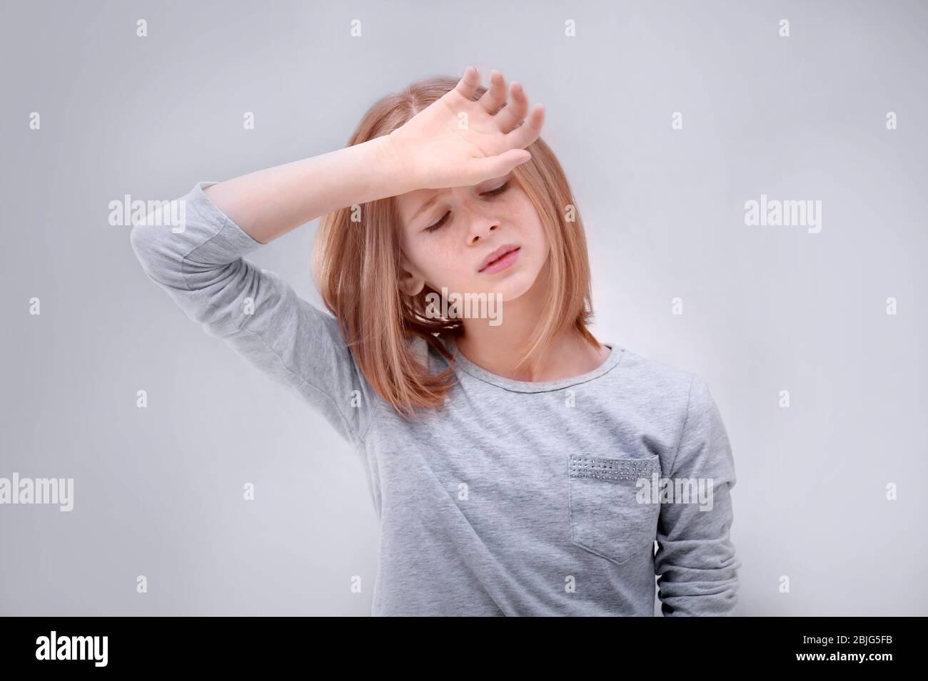 Cute girl suffering from headache on grey background Stock Photo - Alamy