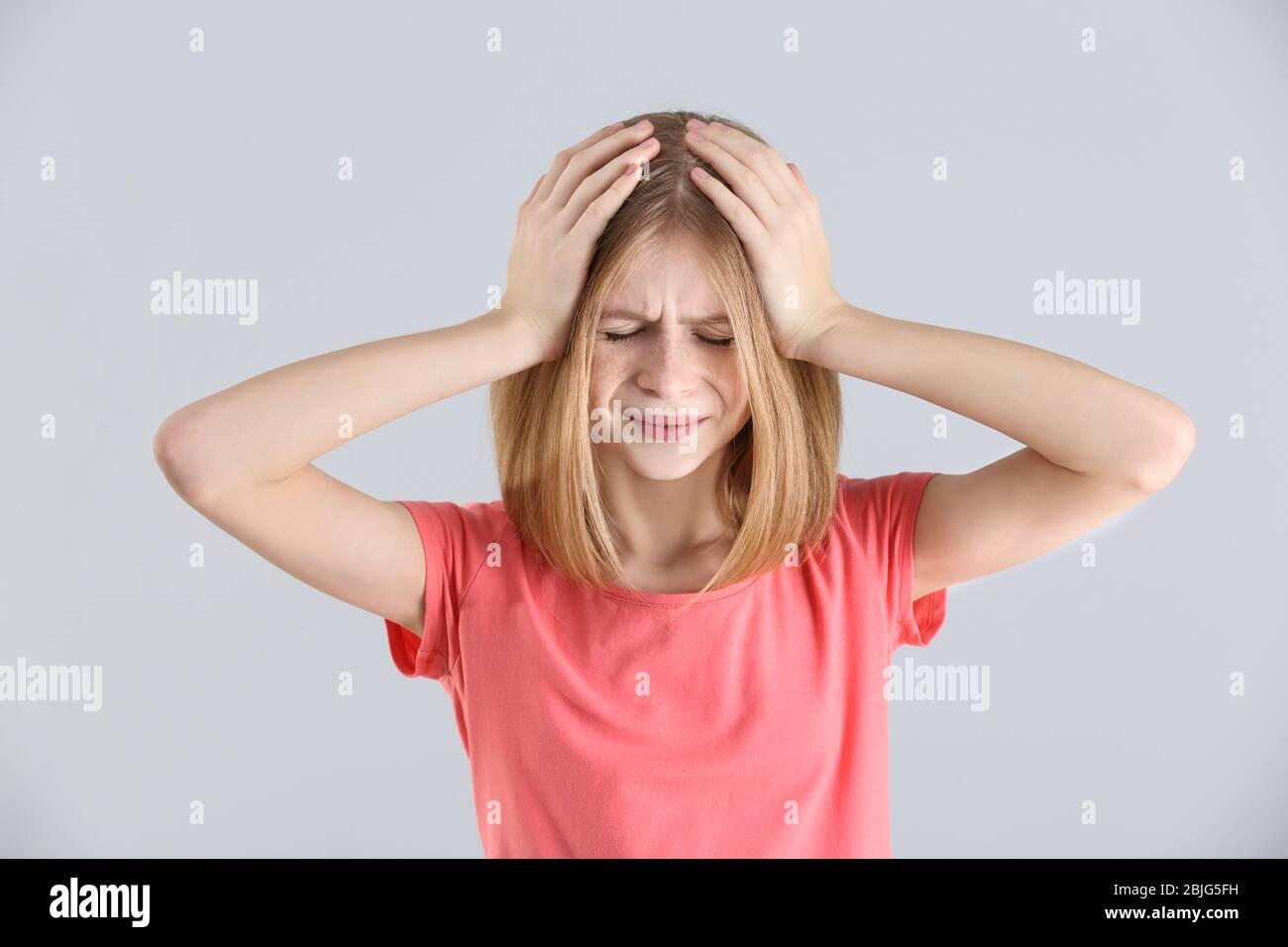 Cute girl suffering from headache on light background Stock Photo - Alamy