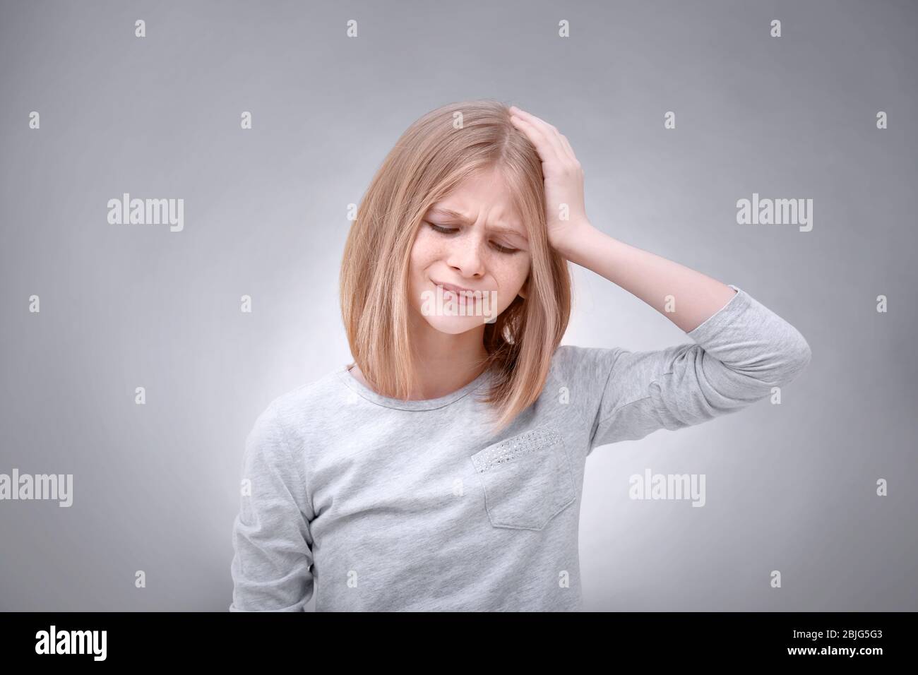 Cute girl suffering from headache on grey background Stock Photo - Alamy