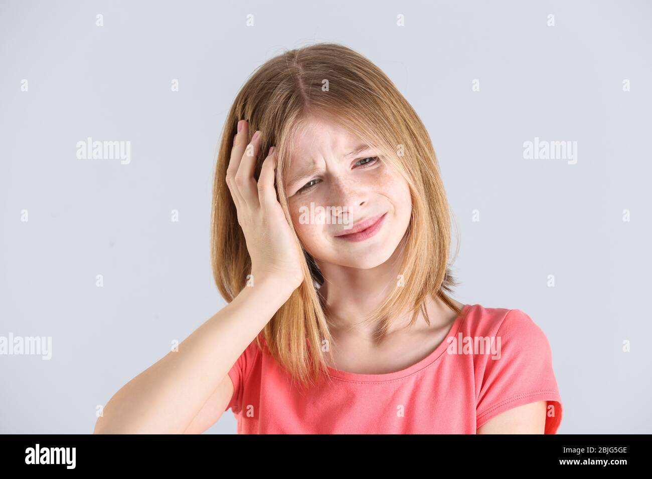 Cute girl suffering from headache on light background Stock Photo - Alamy