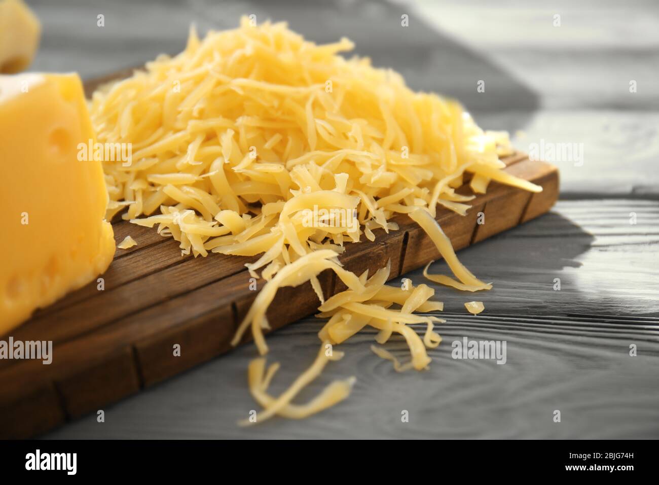 Wooden board with grated cheese on table Stock Photo - Alamy