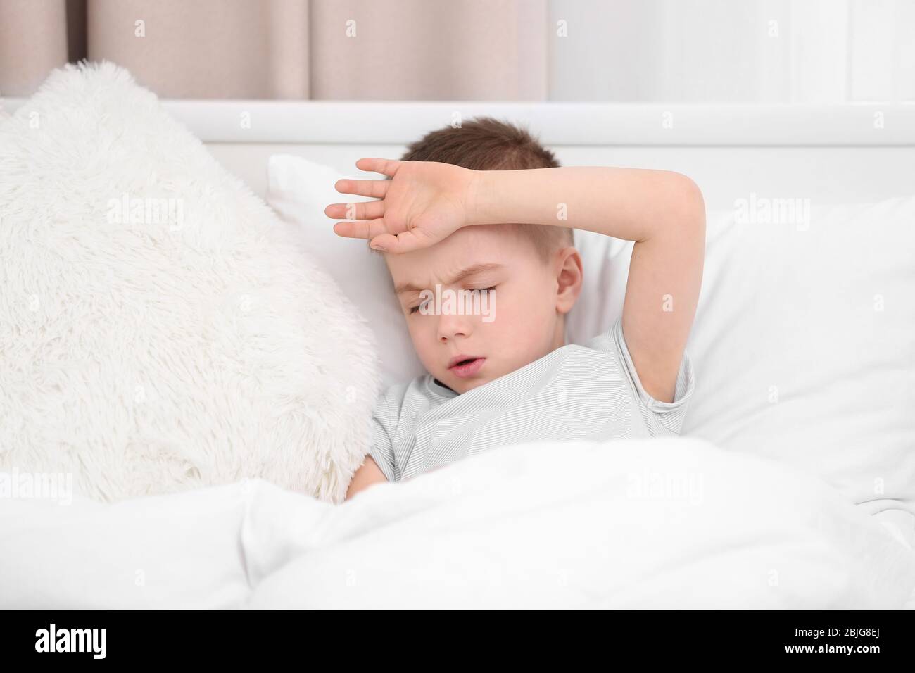 Little boy suffering from headache while lying in bed at home Stock ...