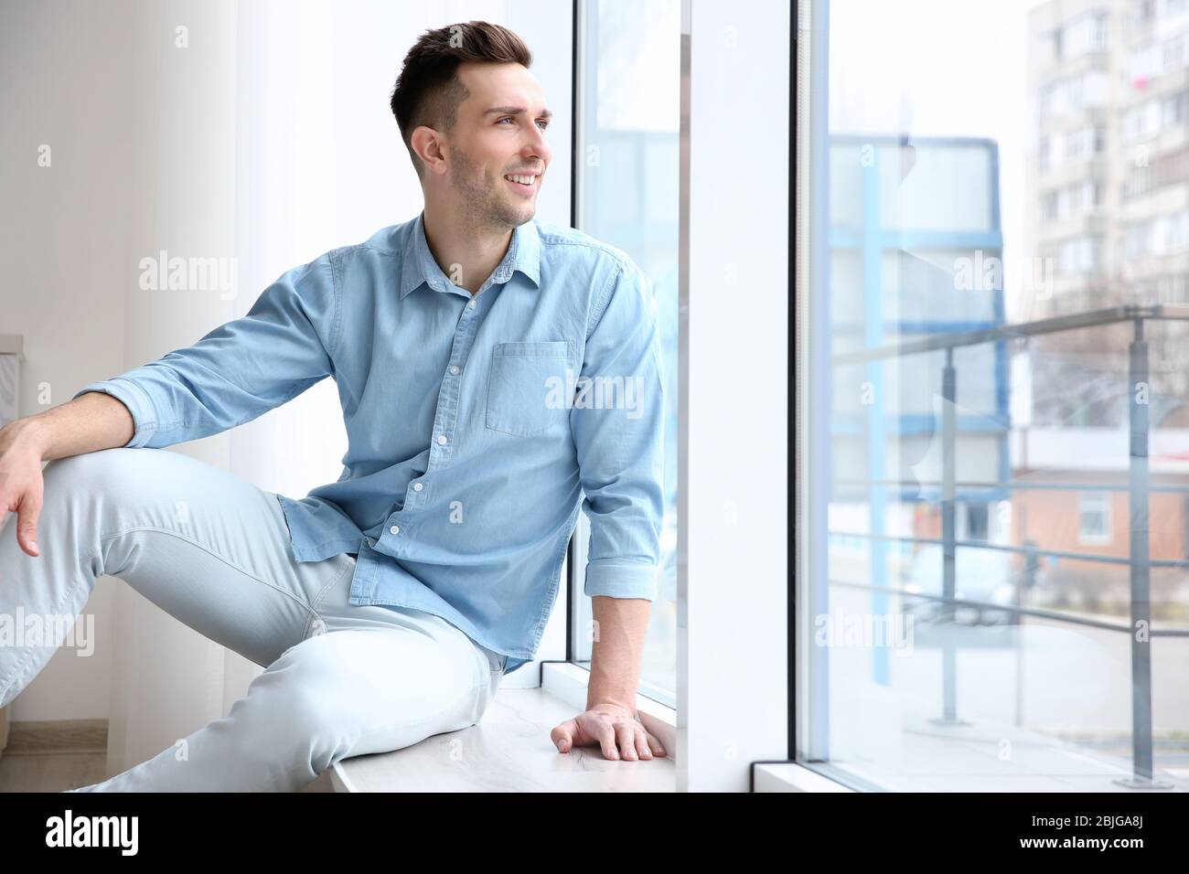 Smiling man sitting on sill near big white plastic window Stock Photo ...
