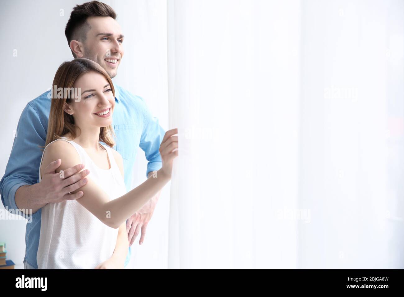 Happy couple standing near big window Stock Photo - Alamy
