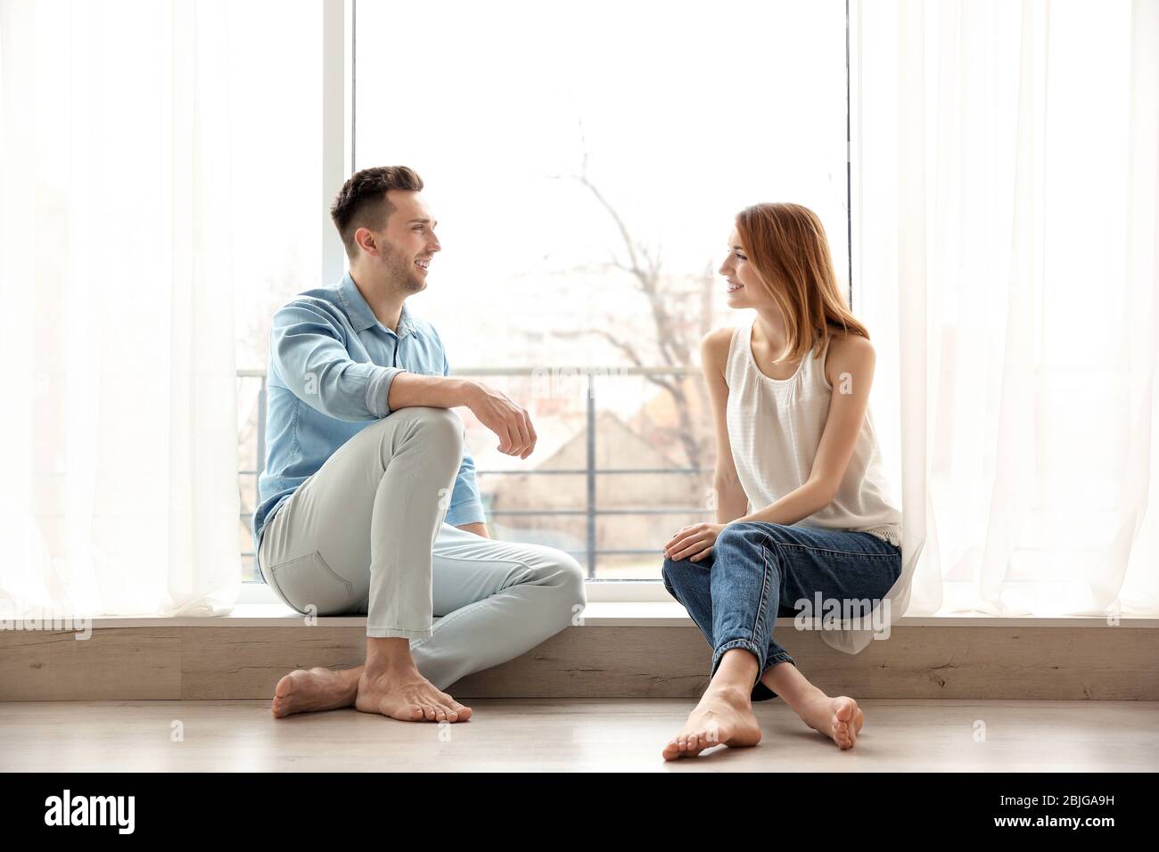 Happy couple sitting on sill near big window Stock Photo - Alamy