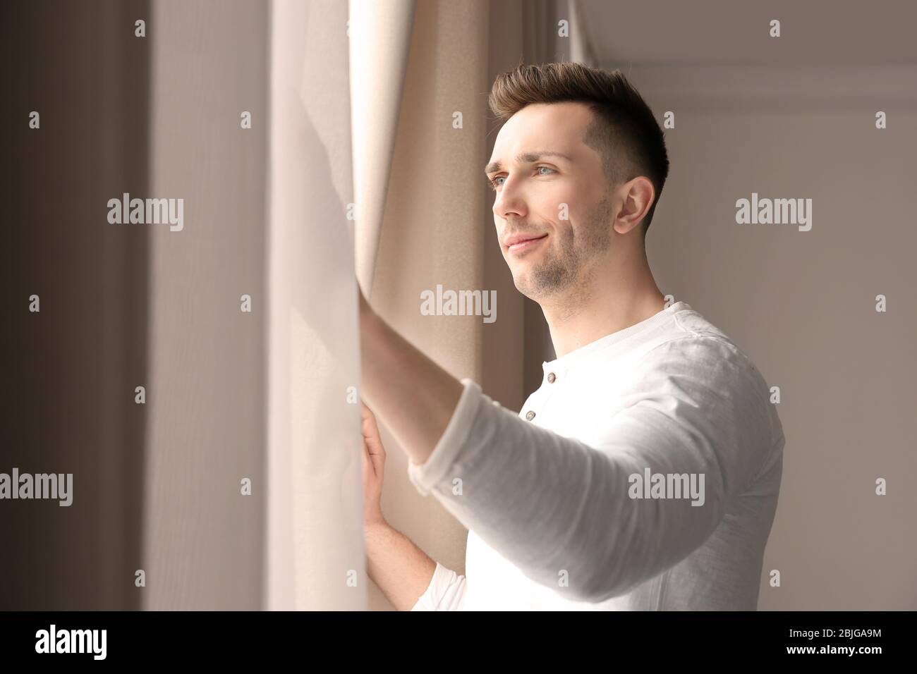 Man opening curtains in light room Stock Photo - Alamy