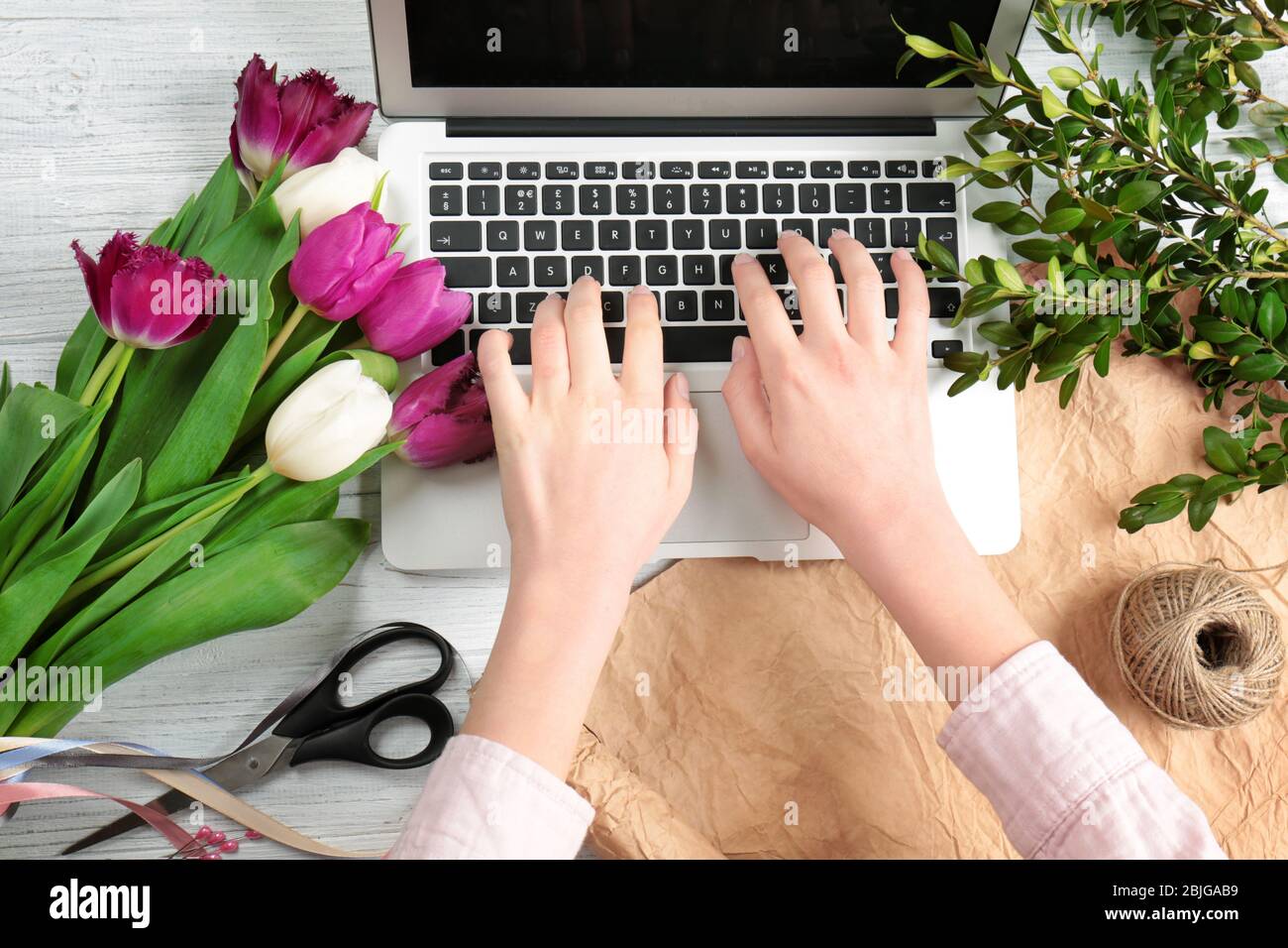 Female florist with laptop and flowers on wooden table Stock Photo - Alamy