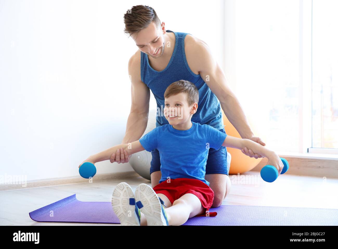 Dad and son doing exercises with dumbbells on mat in gym Stock Photo ...