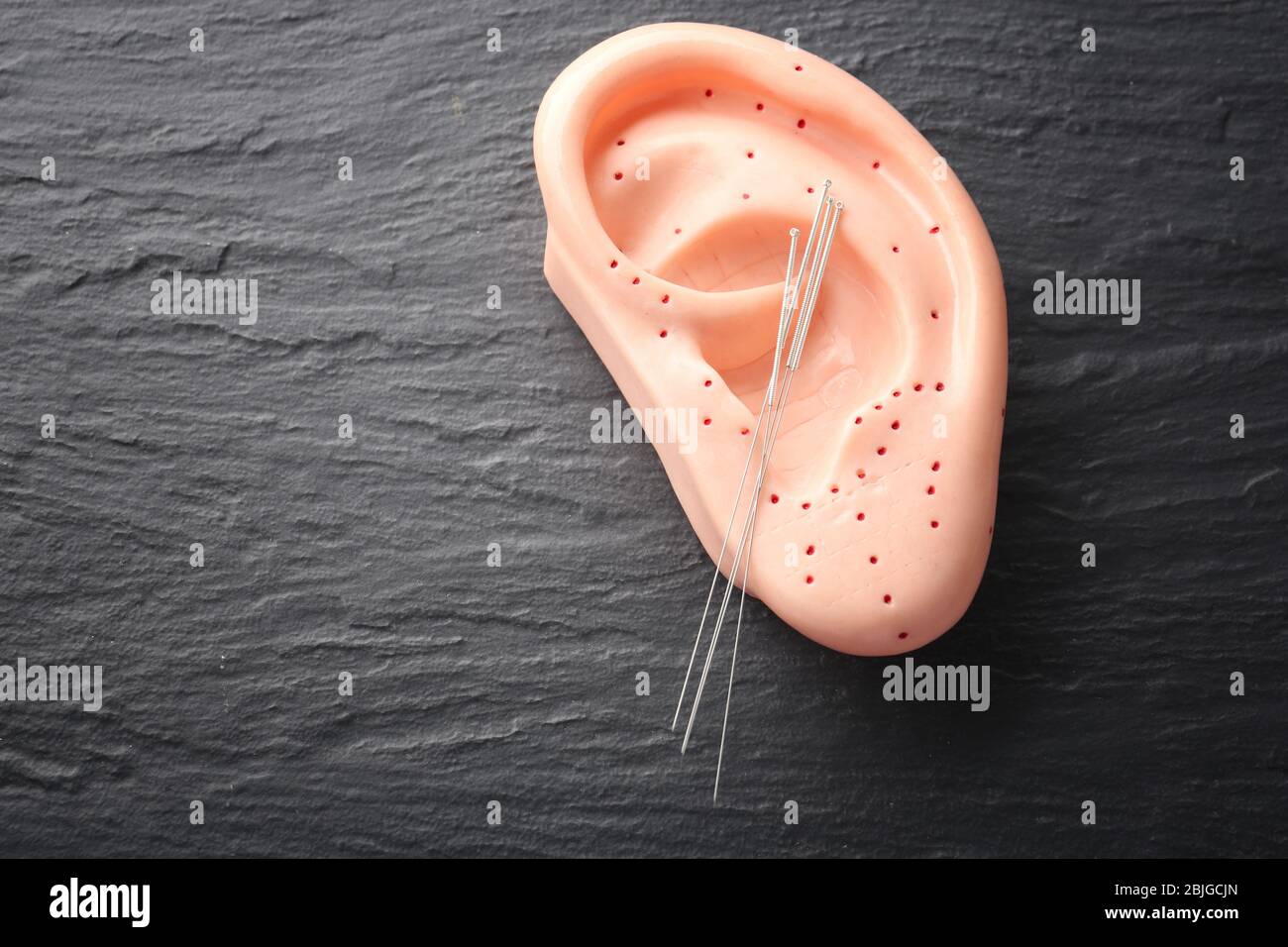Needles for acupuncture and plastic mockup of human ear on dark ...