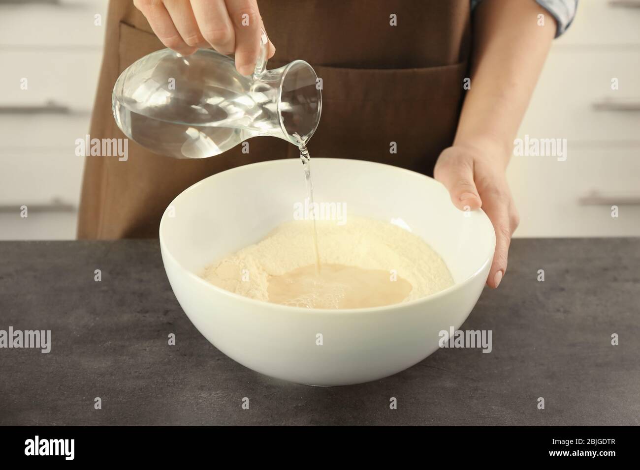 Chef pouring water into glass bowl with flour on table Stock Photo - Alamy