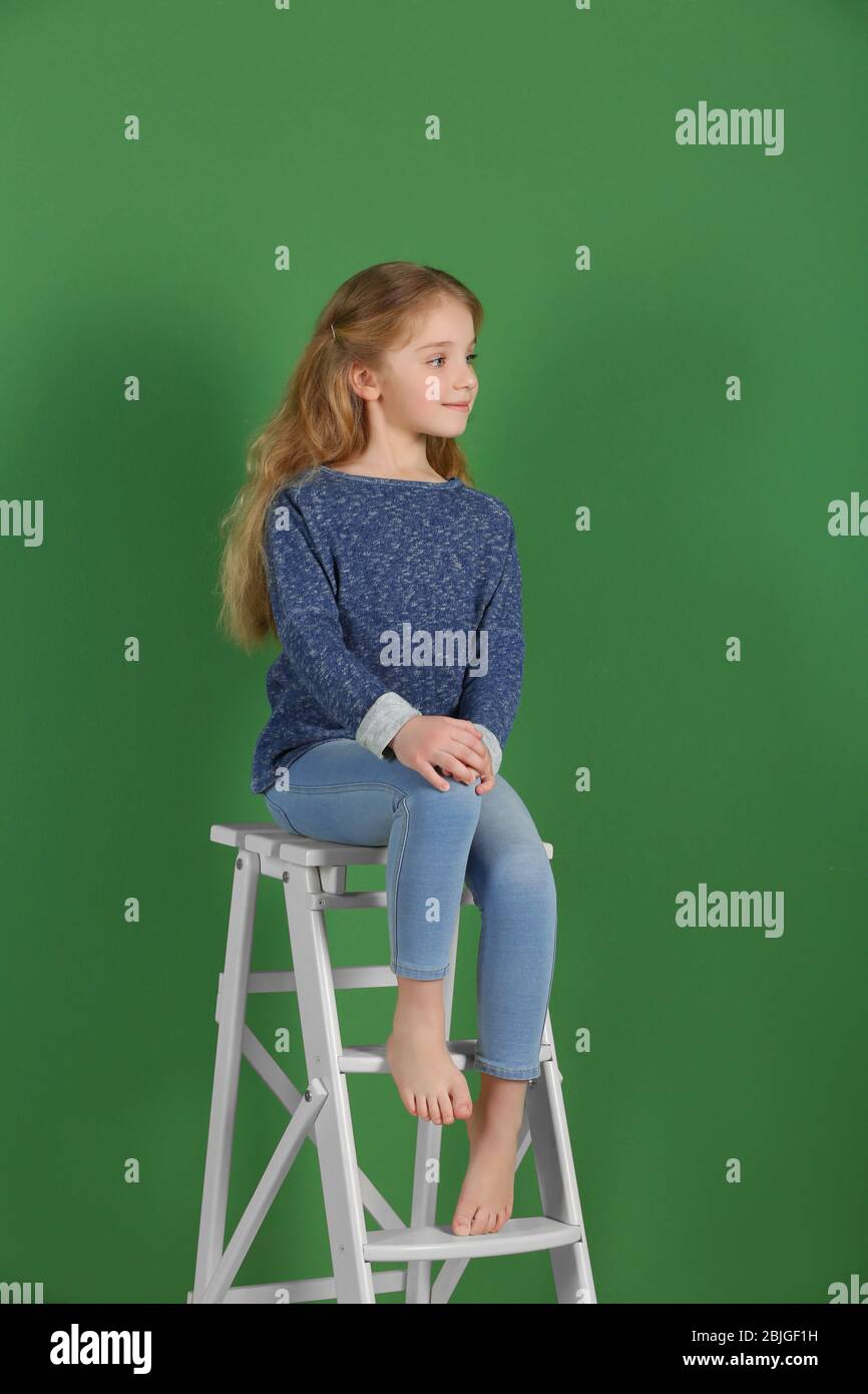 Small girl sitting on step ladder against green background Stock Photo ...
