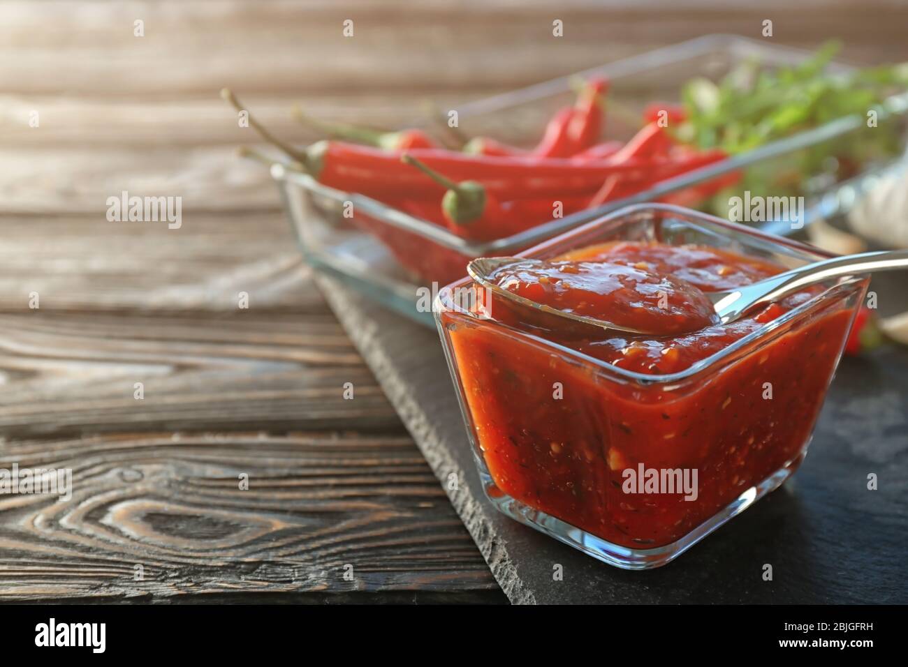 Slate plate and bowl with tasty chili sauce on wooden table, closeup ...