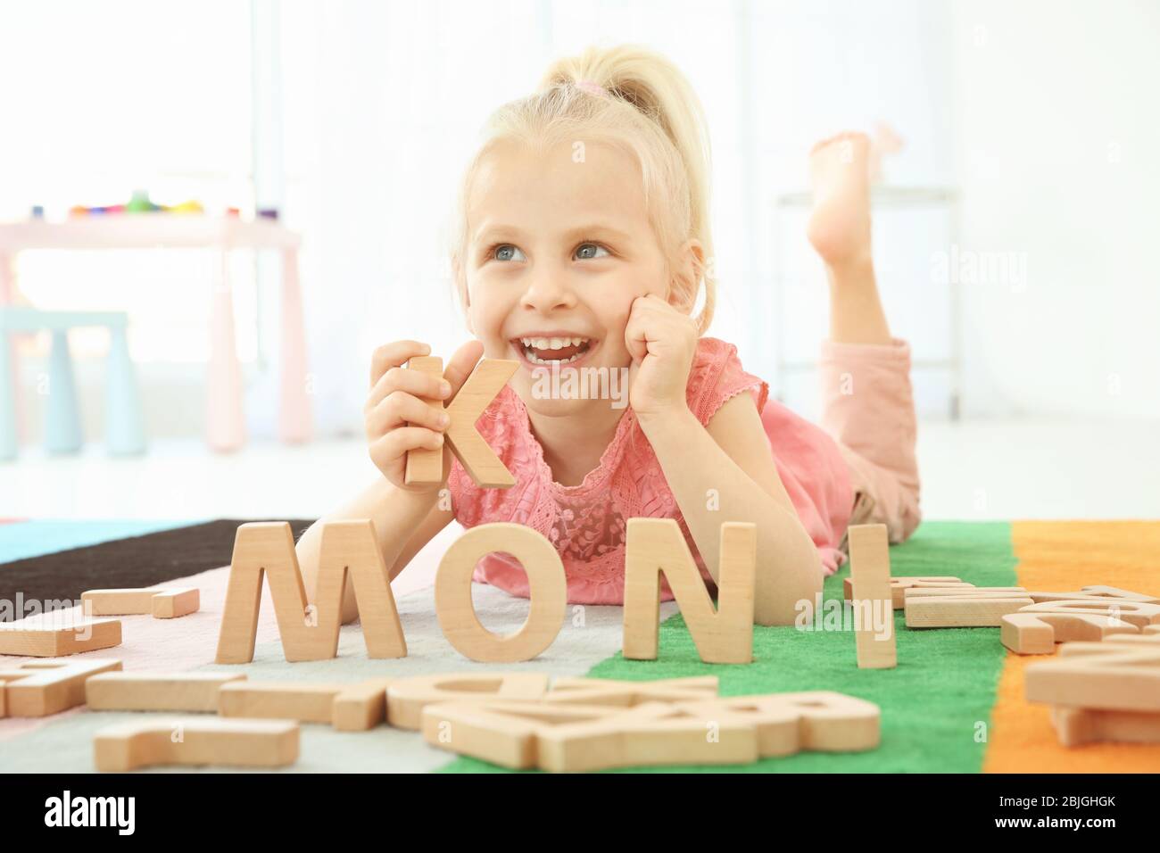 Cute little girl and word MONI composed of wooden letters on floor at ...