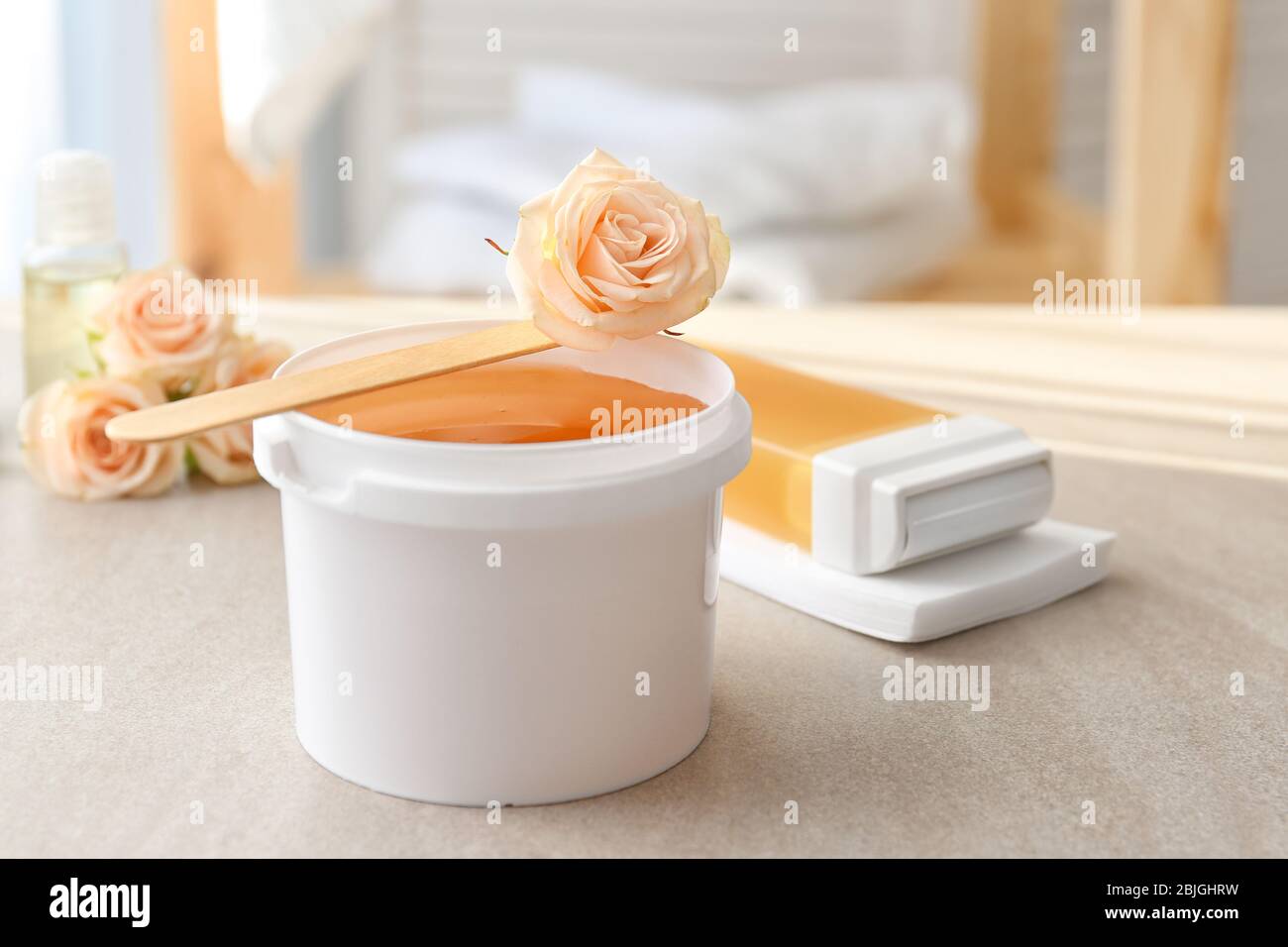 Plastic bucket with sugaring paste, wooden stick and flower on table ...