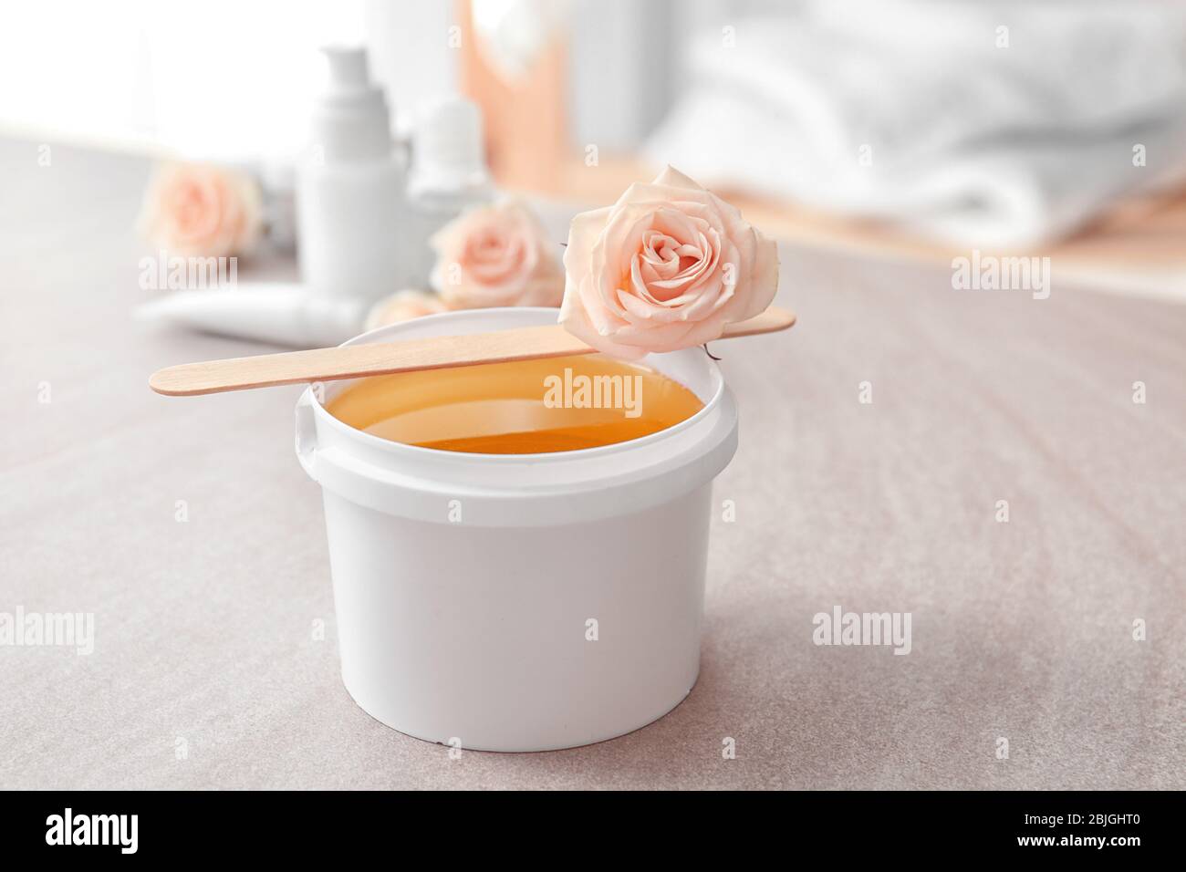 Plastic bucket with sugaring paste, wooden stick and flower on table ...