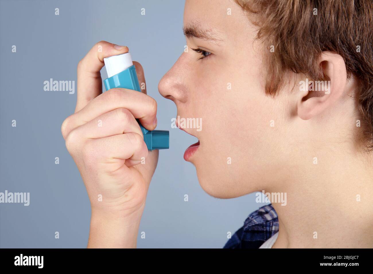 Young boy using inhaler for asthma and respiratory diseases on light ...