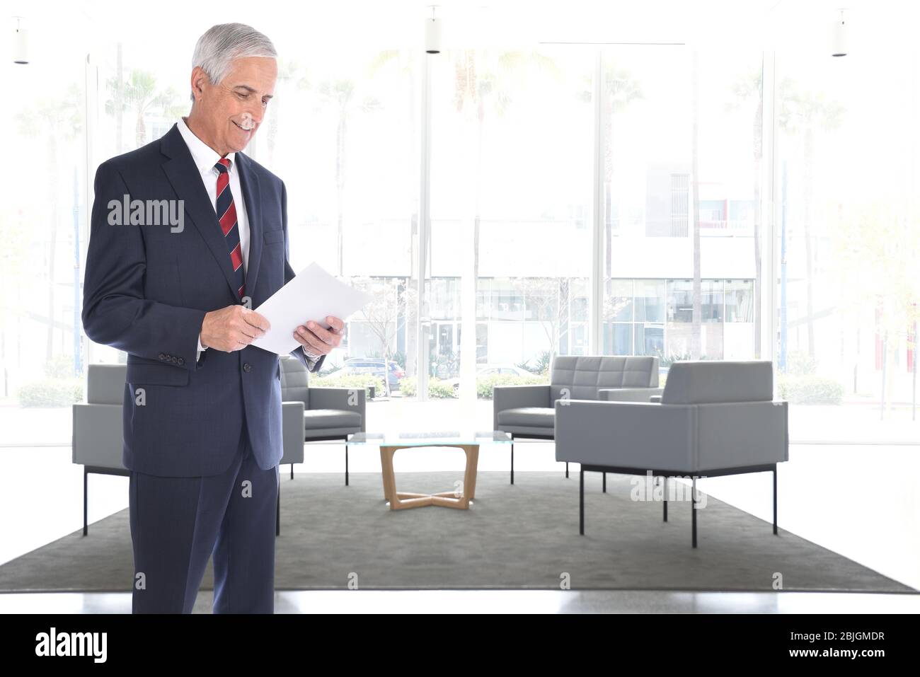 A mature business executive standing in a modern office lobby reading ...