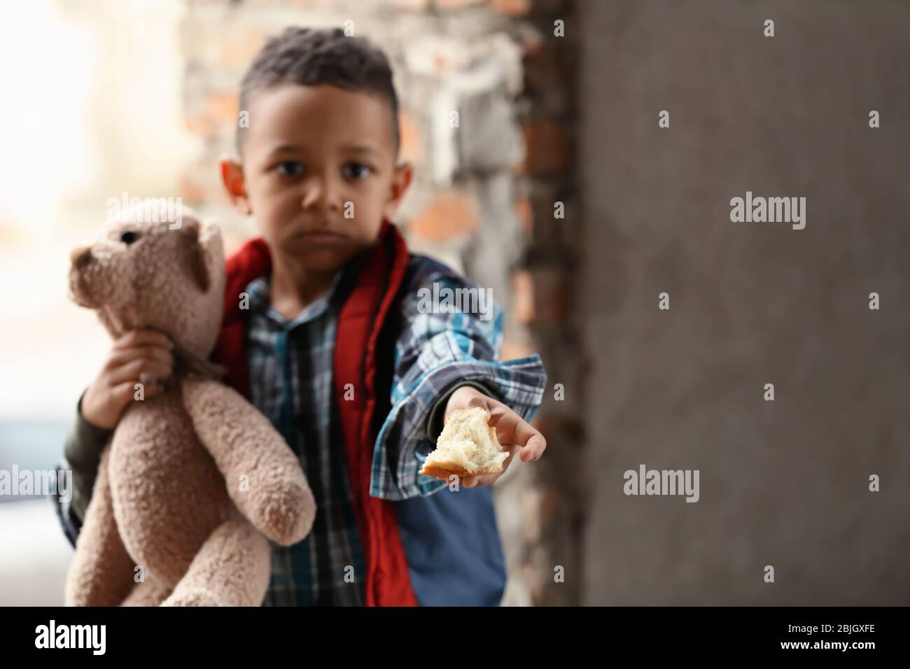Cute little boy with piece of bread in abandoned building. Poverty ...