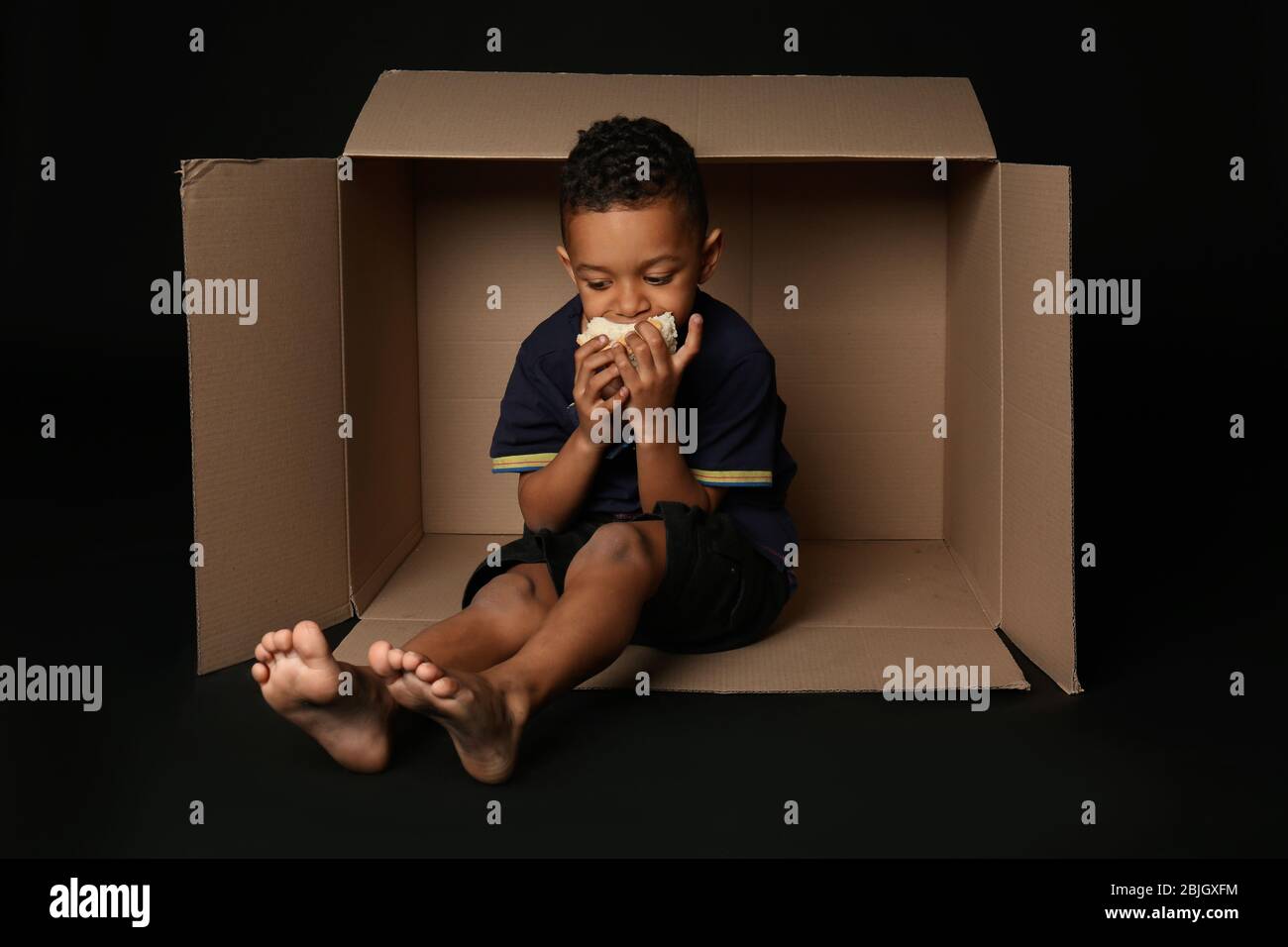 Cute little boy living in box on dark background. Poverty concept Stock ...