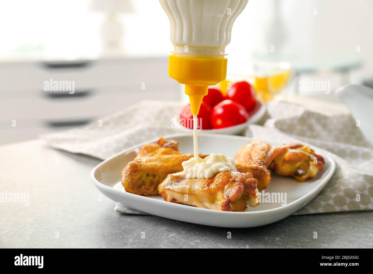 Pouring mayonnaise sauce into plate with tasty chicken wings, closeup ...
