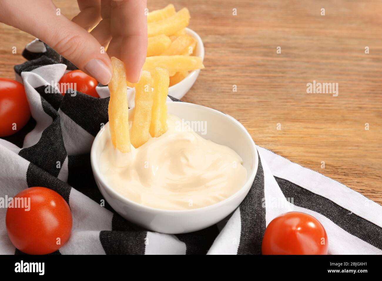 Hand of woman eating French fries with tasty mayonnaise sauce, closeup ...