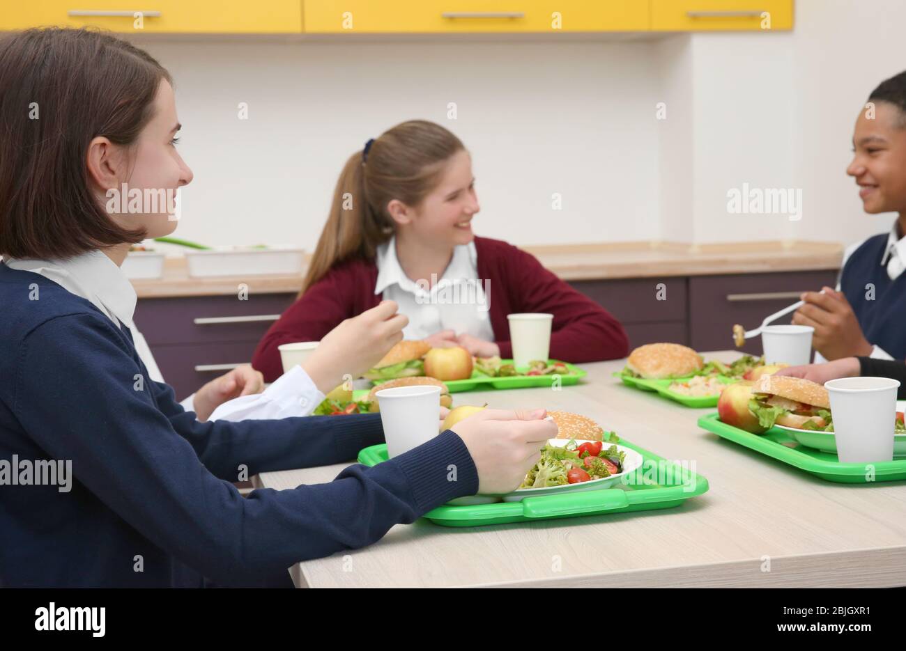 Children sitting at table in school cafeteria while eating lunch Stock ...