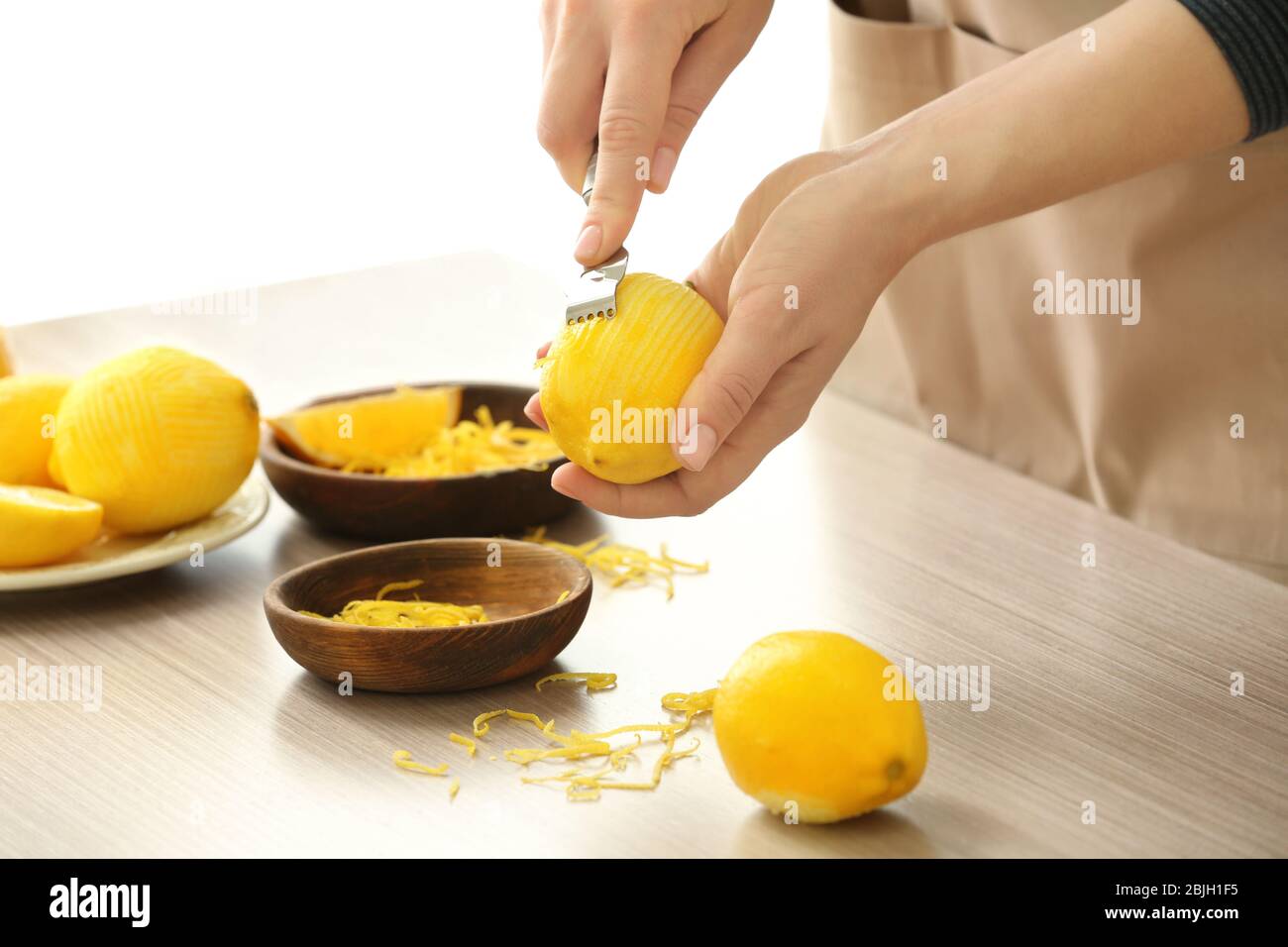 Woman taking off lemon peel with zester over table Stock Photo - Alamy