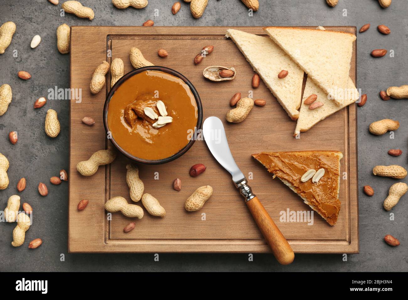 Wooden board with delicious peanut butter, toasts and nuts on table ...