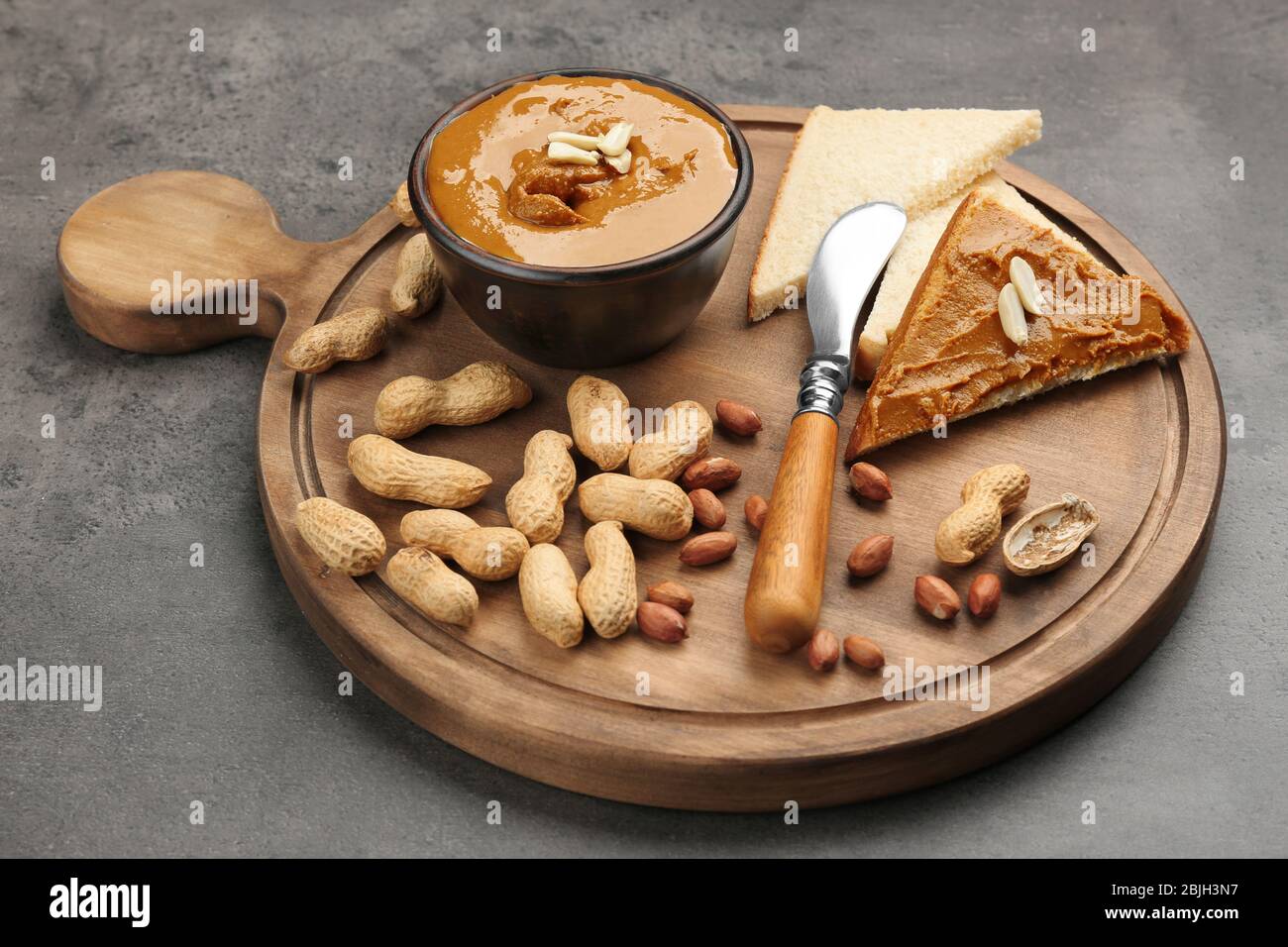 Wooden board with delicious peanut butter, toasts and nuts on table ...