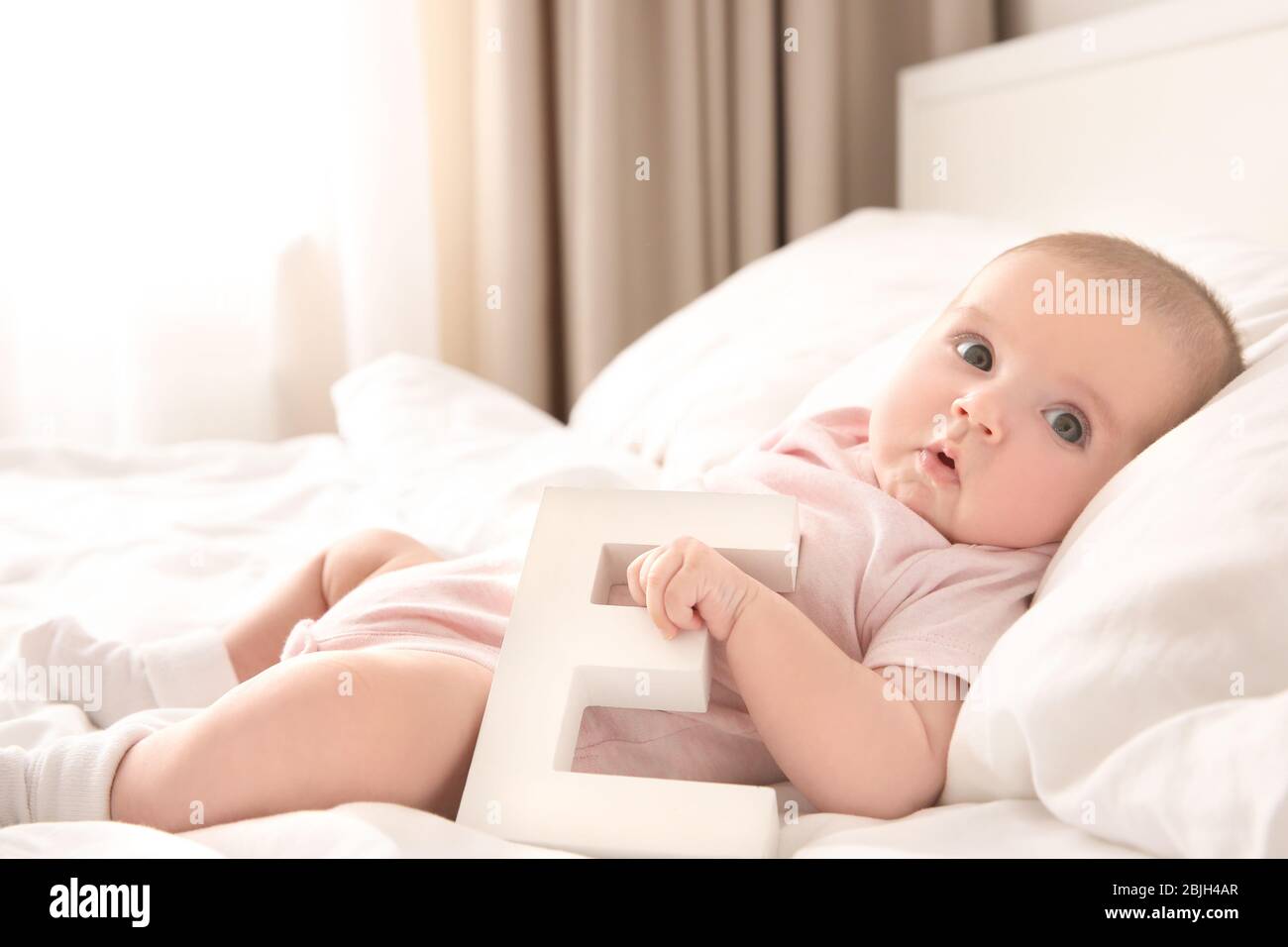 Cute little baby with letter E lying on bed. Choosing name concept ...