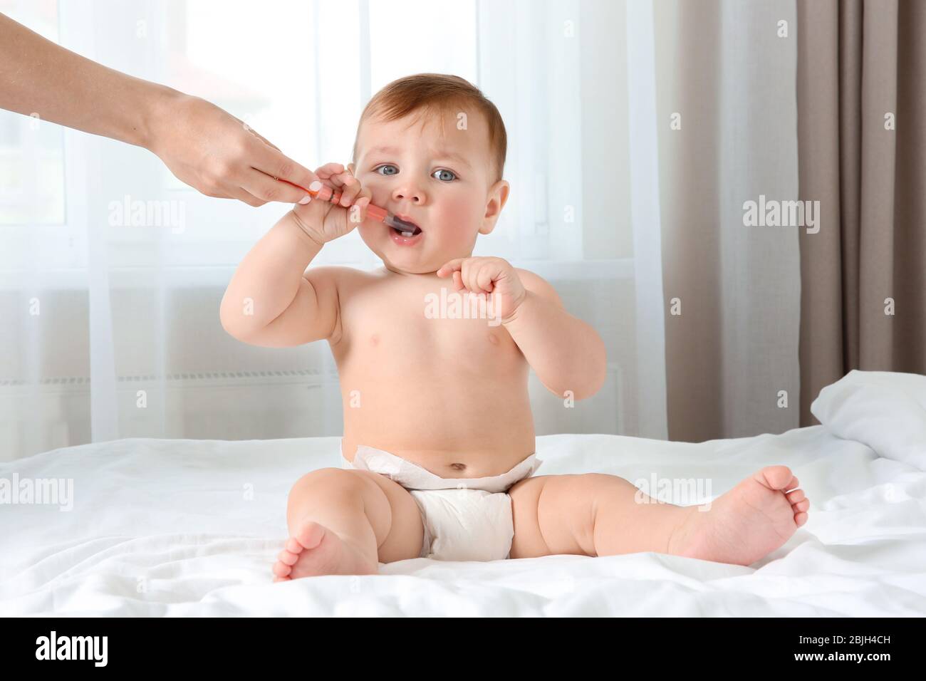 Mother holding oral dosing syringe and cute little baby sitting on bed ...