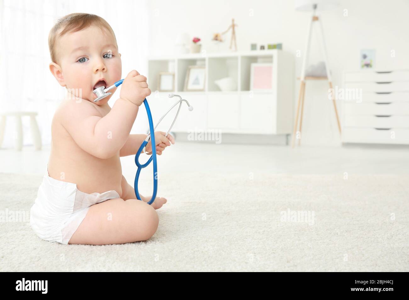 Cute little baby with stethoscope sitting on floor at home. Health care ...
