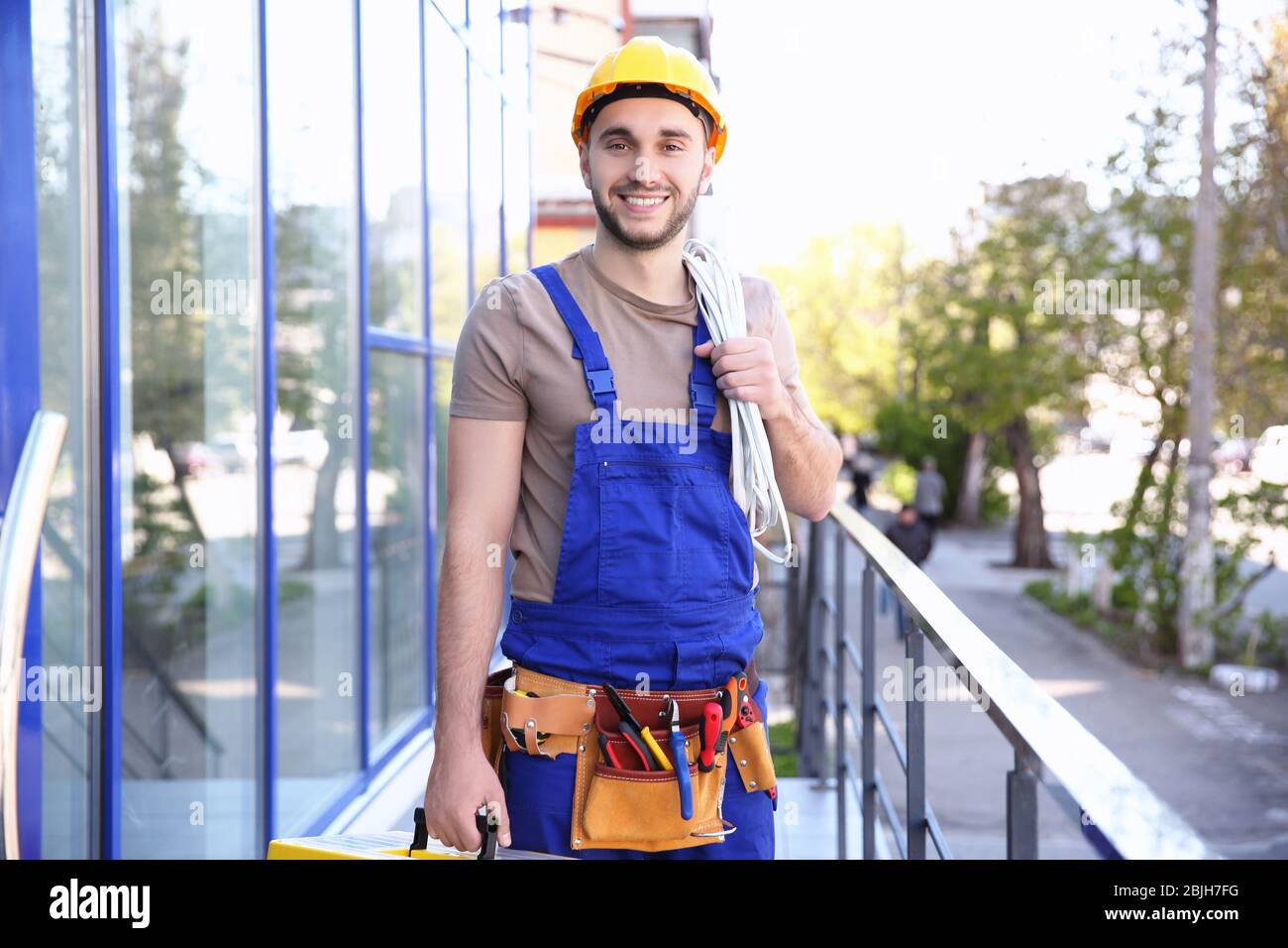 Young smiling electrician holding bunch of wires outdoors Stock Photo ...