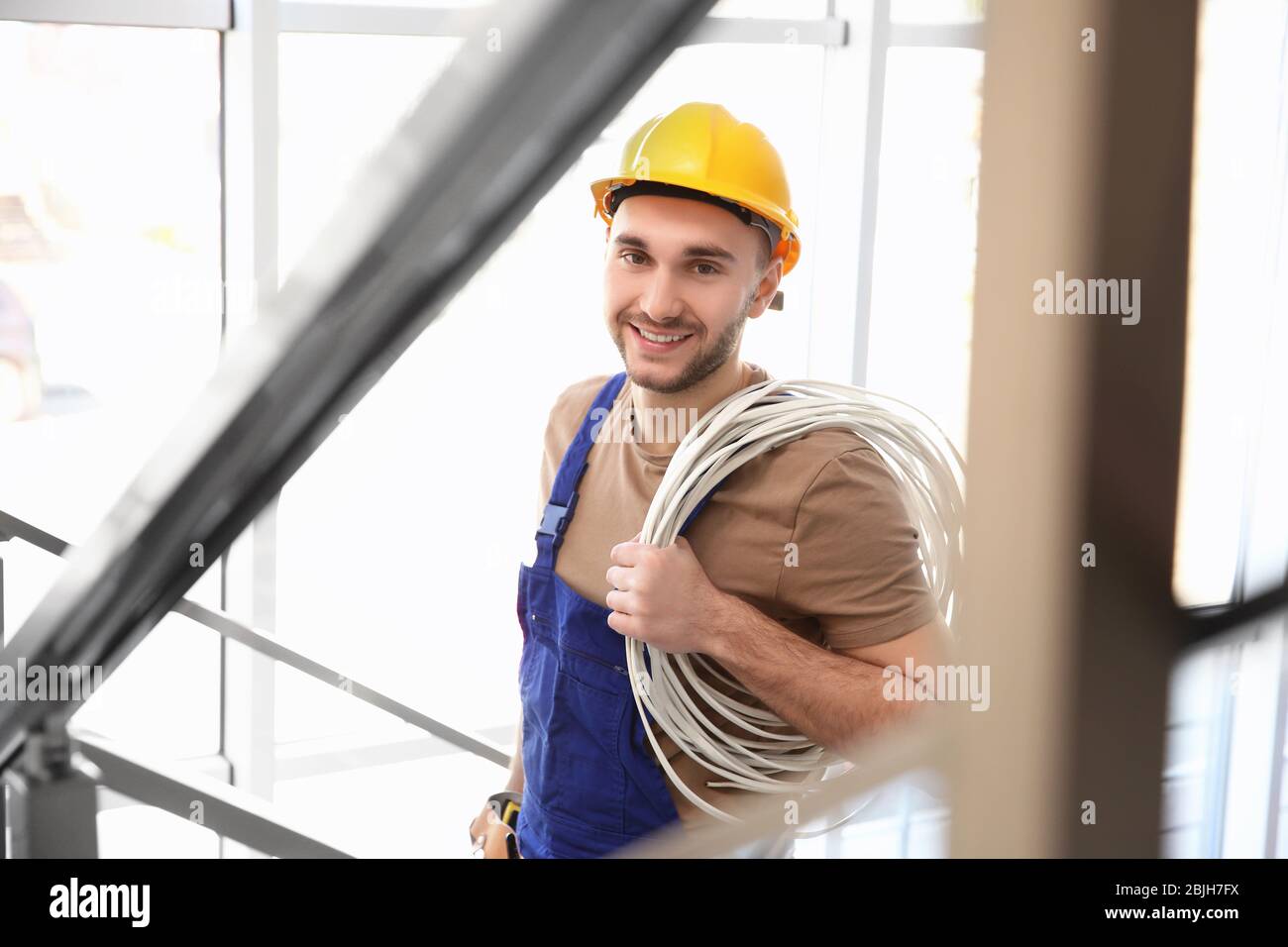 Young smiling electrician holding bunch of wires in light room Stock ...