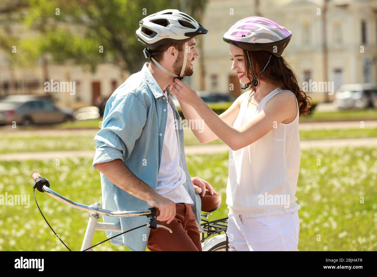 Young woman helping her boyfriend to put on bicycle helmet in park Stock Photo - Alamy