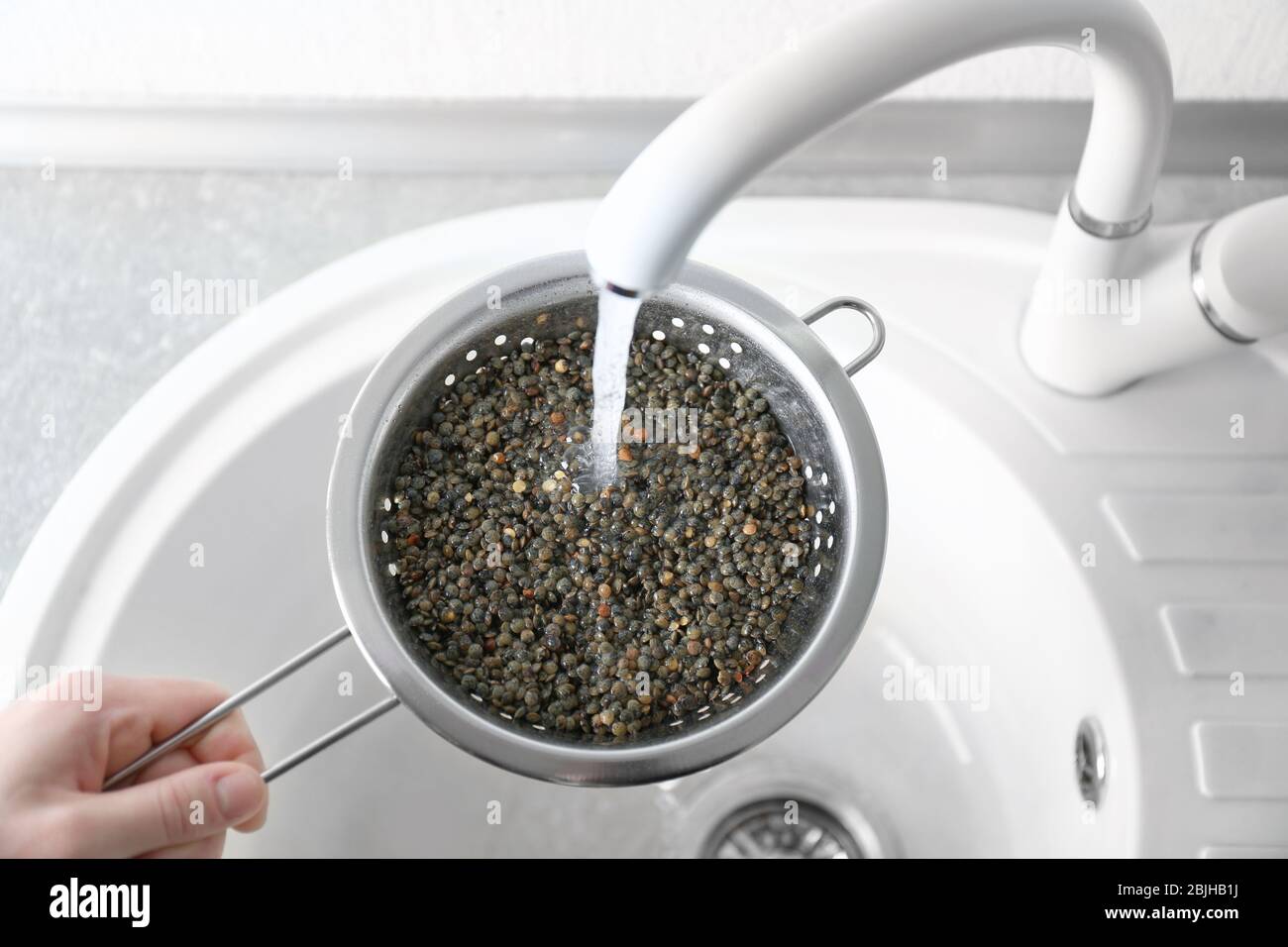 Washing raw lentils with tap water before cooking in kitchen Stock ...