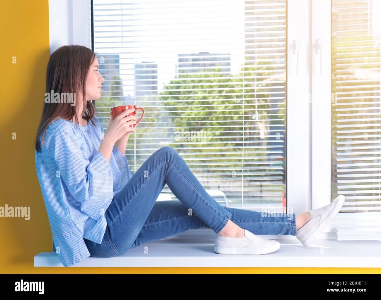 Beautiful young girl looking in window and holding cup of coffee or tea ...