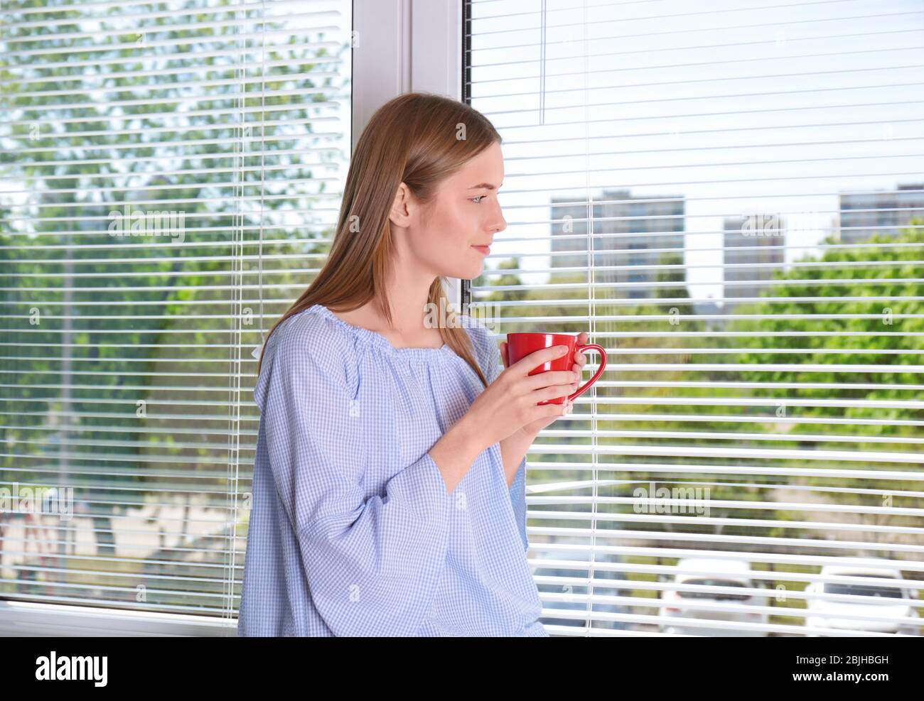 Beautiful young girl looking in window and holding cup of coffee or tea ...