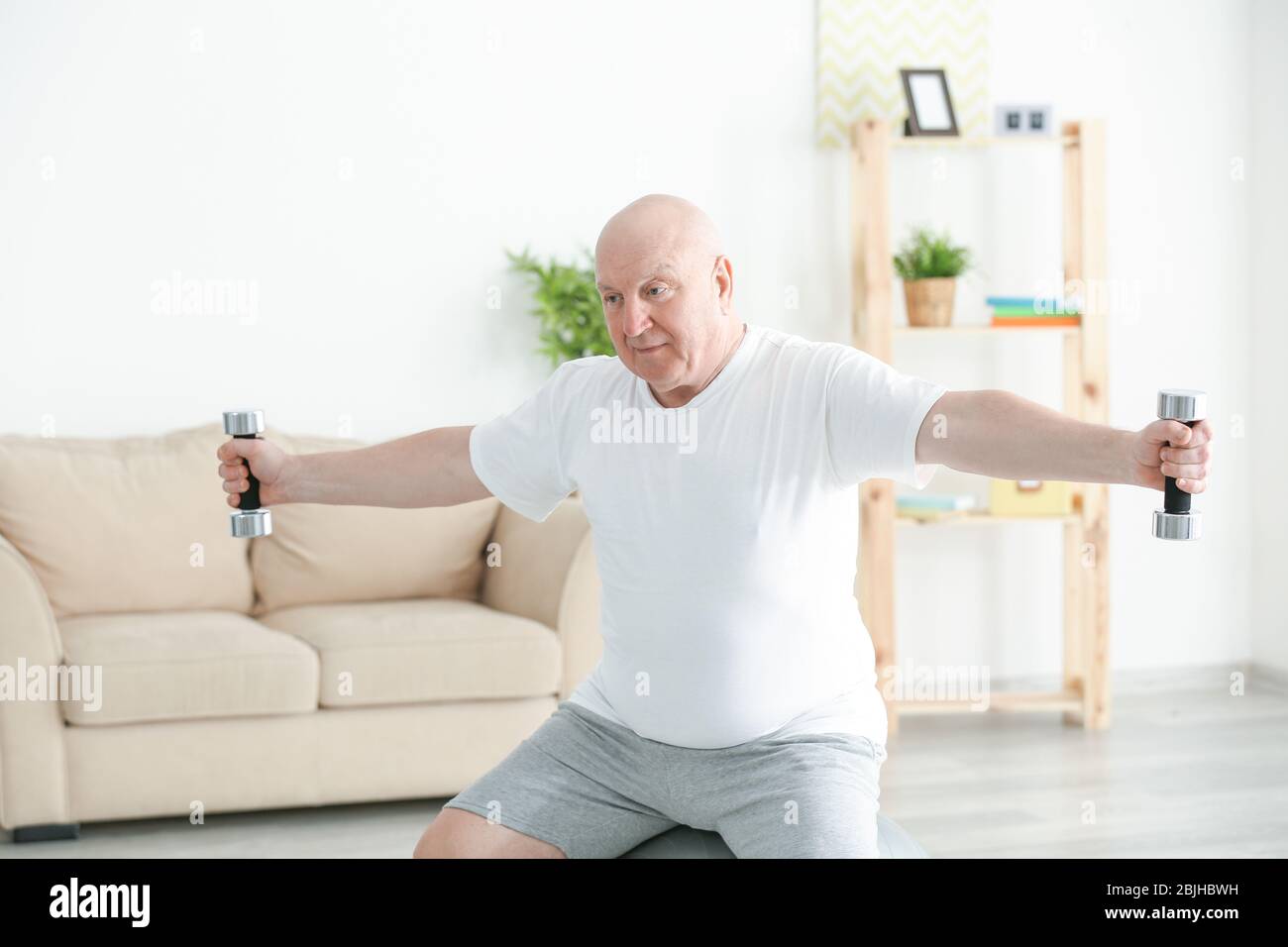 Fat senior man training with dumbbells at home. Weight loss concept ...