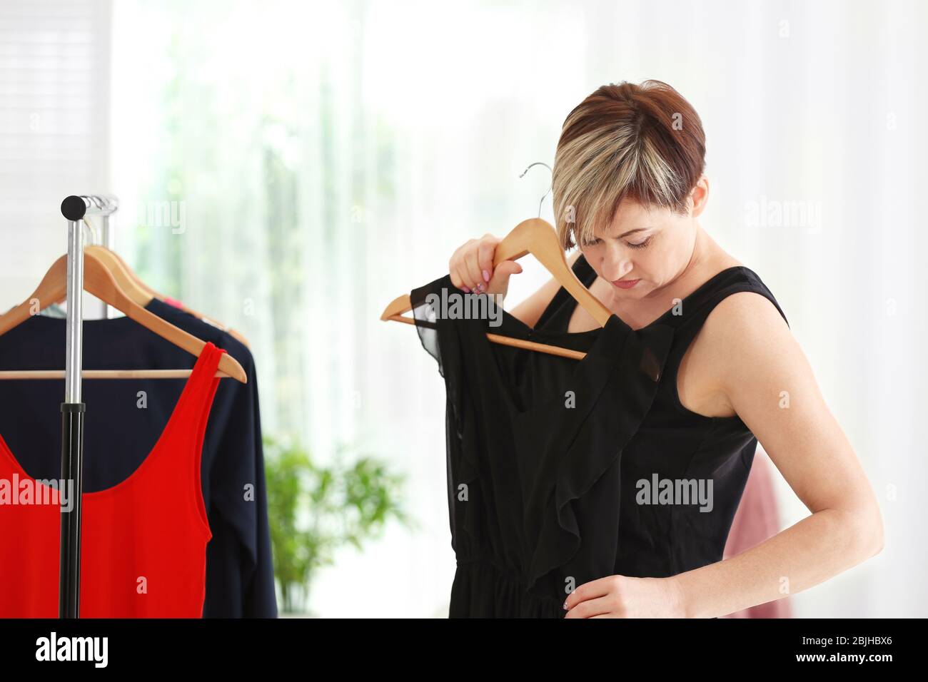 Mature woman near rack with small-sized clothes at home. Weight loss ...