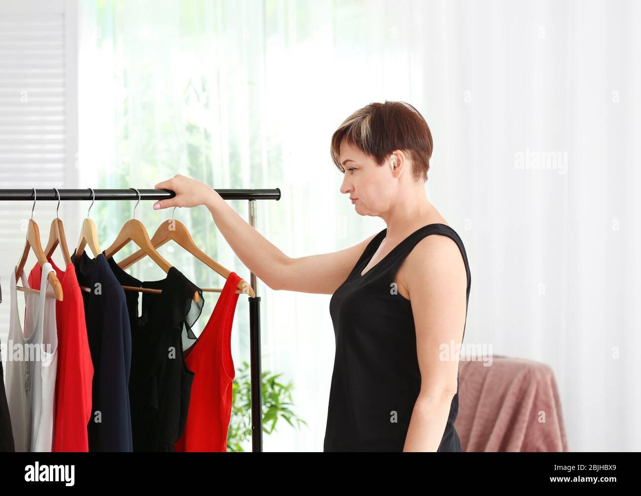 Mature woman near rack with small-sized clothes at home. Weight loss ...