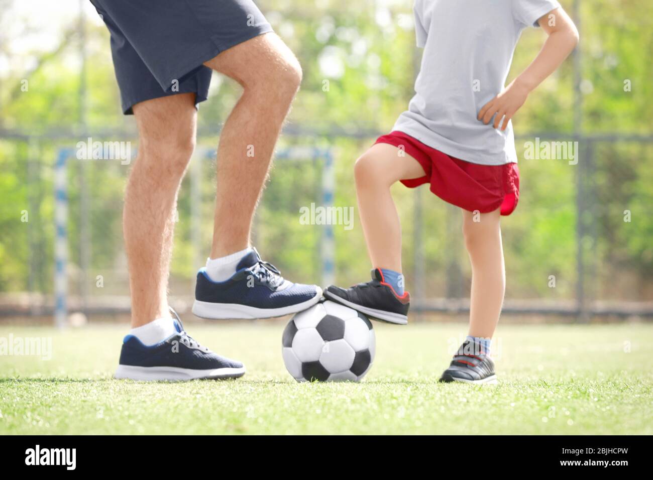 Legs of father and son with ball on soccer pitch Stock Photo - Alamy