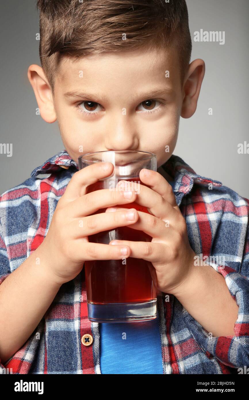 Cute little boy drinking juice on grey background, closeup Stock Photo ...