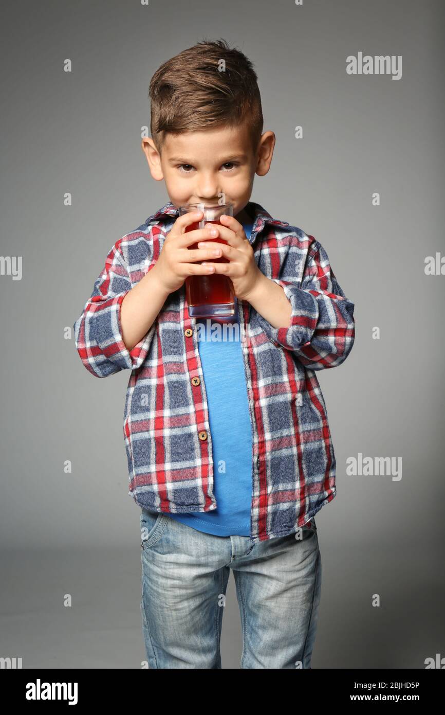 Cute little boy drinking juice on grey background Stock Photo - Alamy