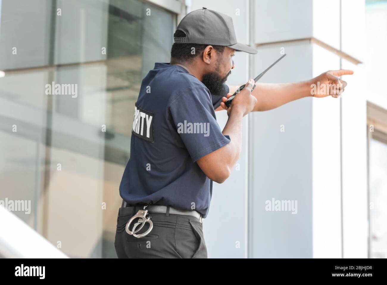 Male security guard using portable radio transmitter near big modern ...