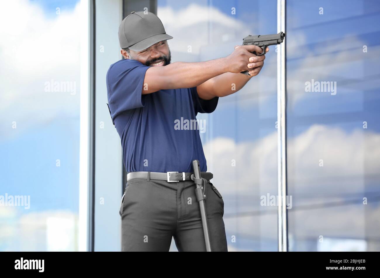 Male security guard taking aim near big modern building Stock Photo - Alamy