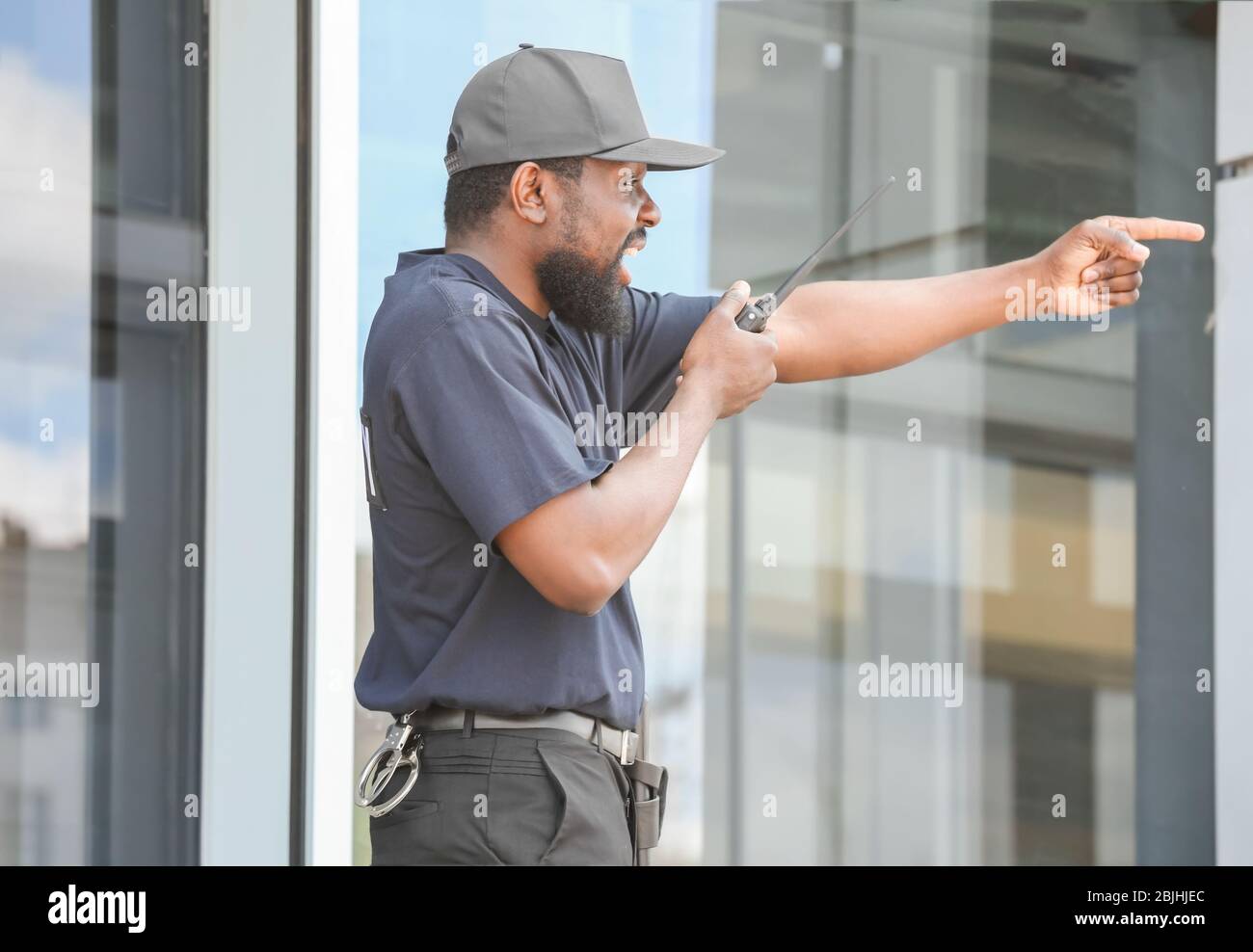 Male security guard using portable radio transmitter near big modern ...