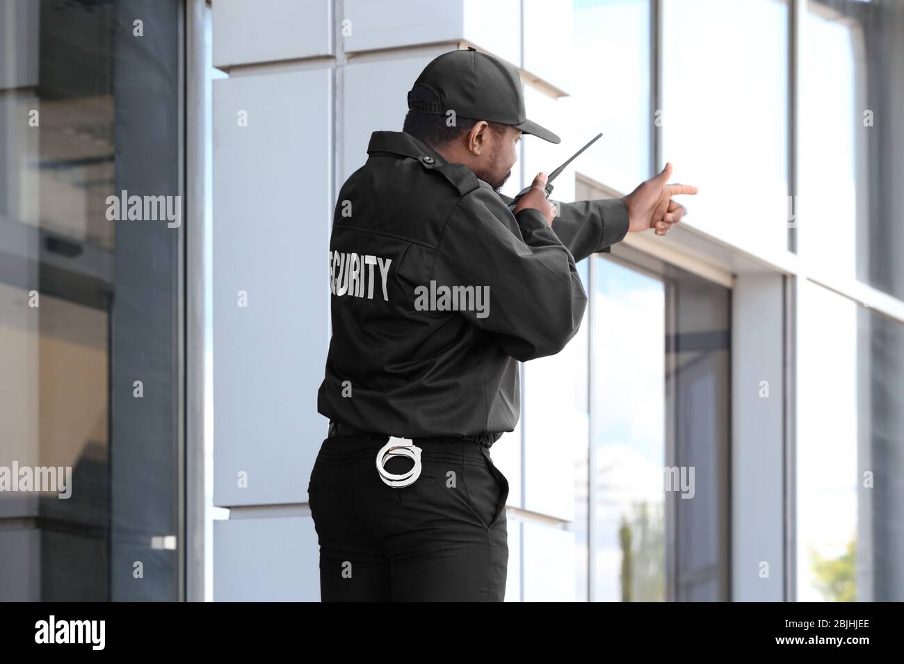 Male security guard using portable radio transmitter near big modern ...